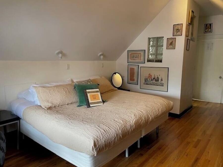 Quarto com cama, mesa de cabeceira, luminária na parede e quadros emoldurados.