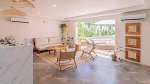 Um hall de hotel moderno com uma recepção de mármore, um sofá, cadeiras de vime, uma mesa de centro de madeira e uma grande janela com vista para o exterior.