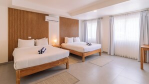 Quarto de hotel com duas camas de madeira, cabeceiras de madeira, uma pequena mesa e uma janela com cortinas.
