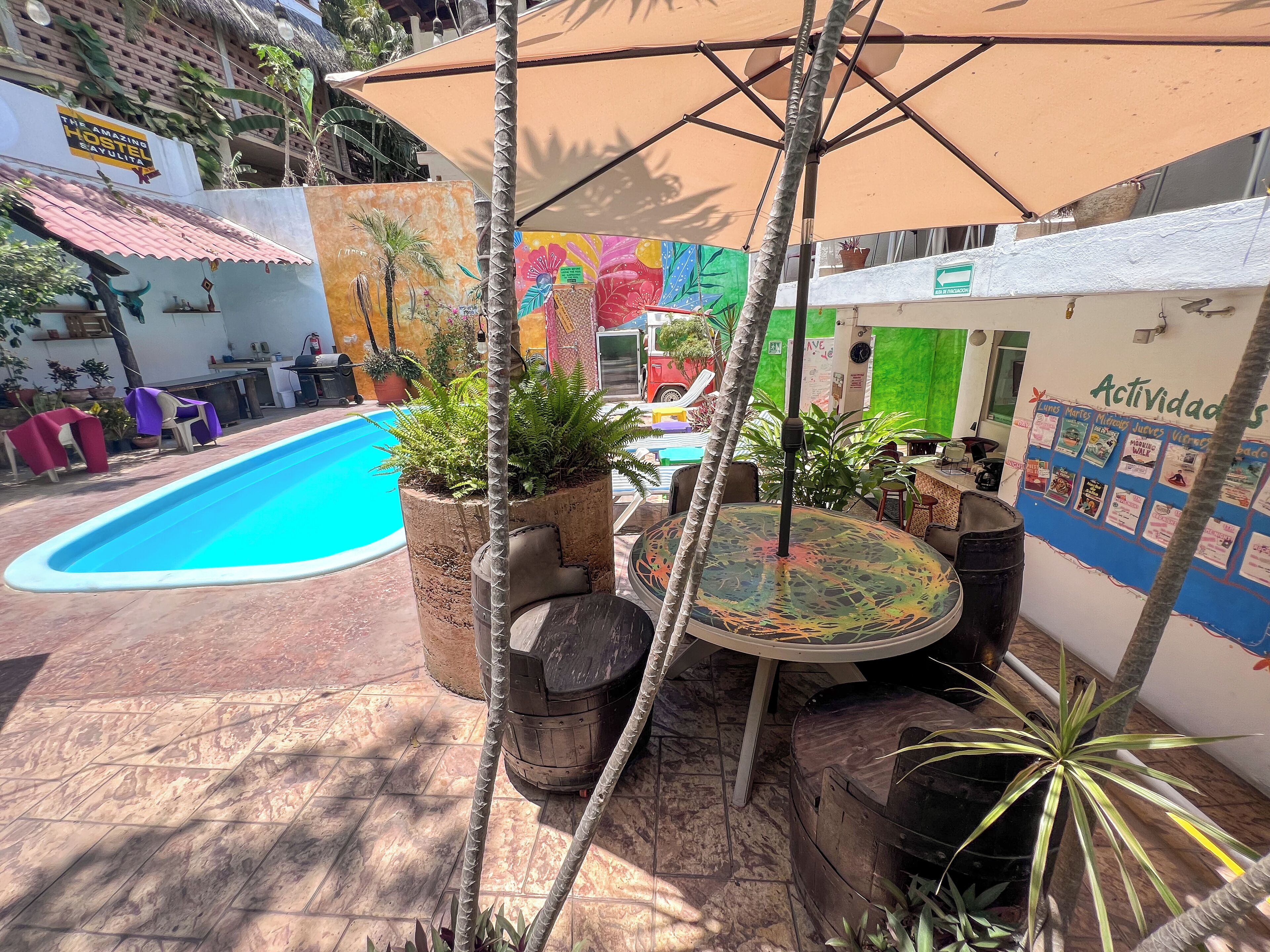 Uma área de piscina com piso ladrilhado, uma mesa redonda com cadeiras e um mural.