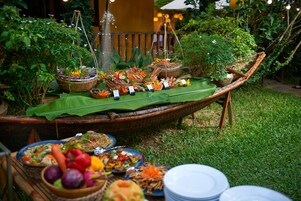 Um barco cheio de diversos alimentos e cestas, rodeado por vegetação e um jardim.