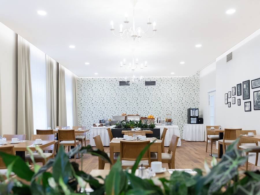 Uma área de refeições com mesas e cadeiras de madeira, um buffet com comida e bebidas, e uma parede com quadros.