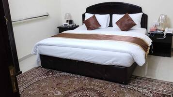 Uma cama bem arrumada com colcha marrom e branca, cabeceira escura e tapete estampado no chão.