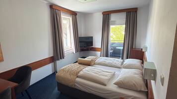 Quarto de hotel com cama, escrivaninha, cadeira, televisão e vista para o exterior.