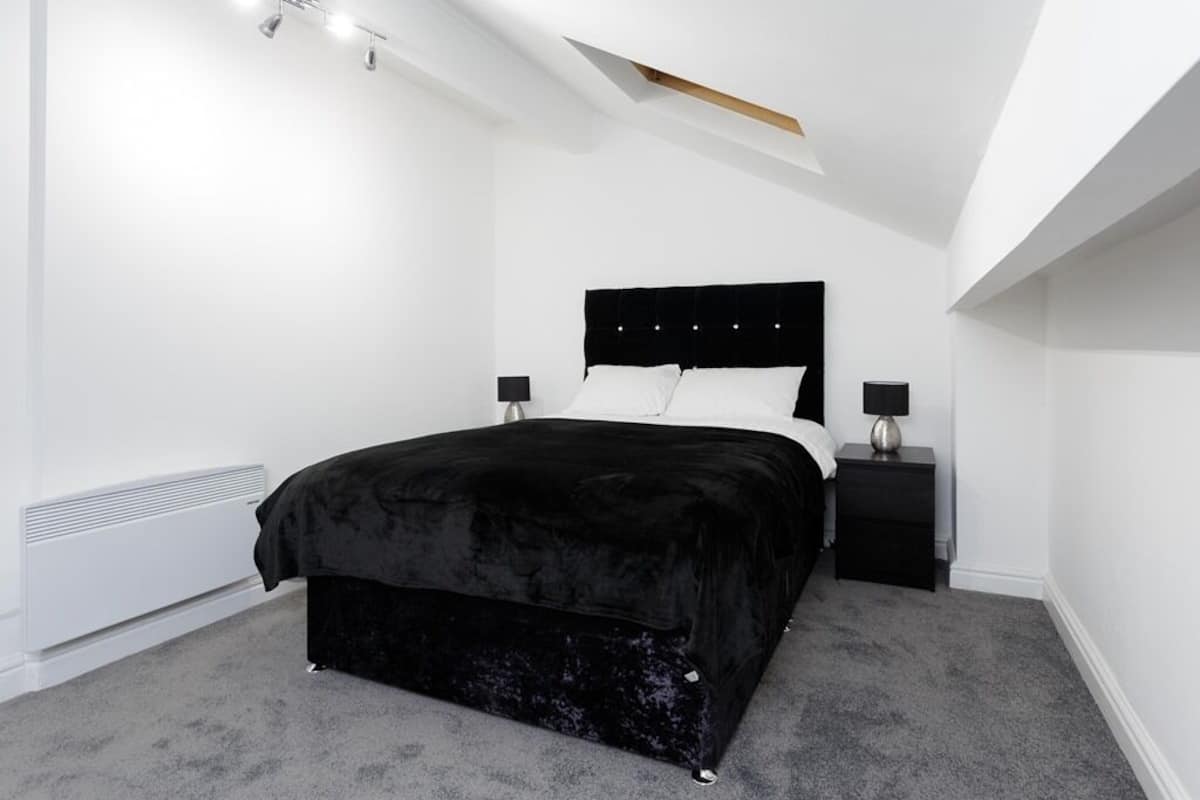 Um quarto moderno com uma cama preta, paredes brancas e teto inclinado.