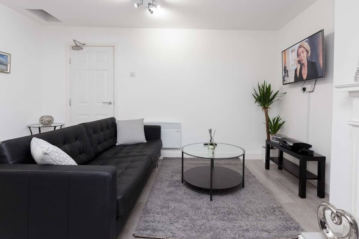 Uma sala de estar moderna com um sofá preto, uma mesa de centro de vidro e uma porta branca.
