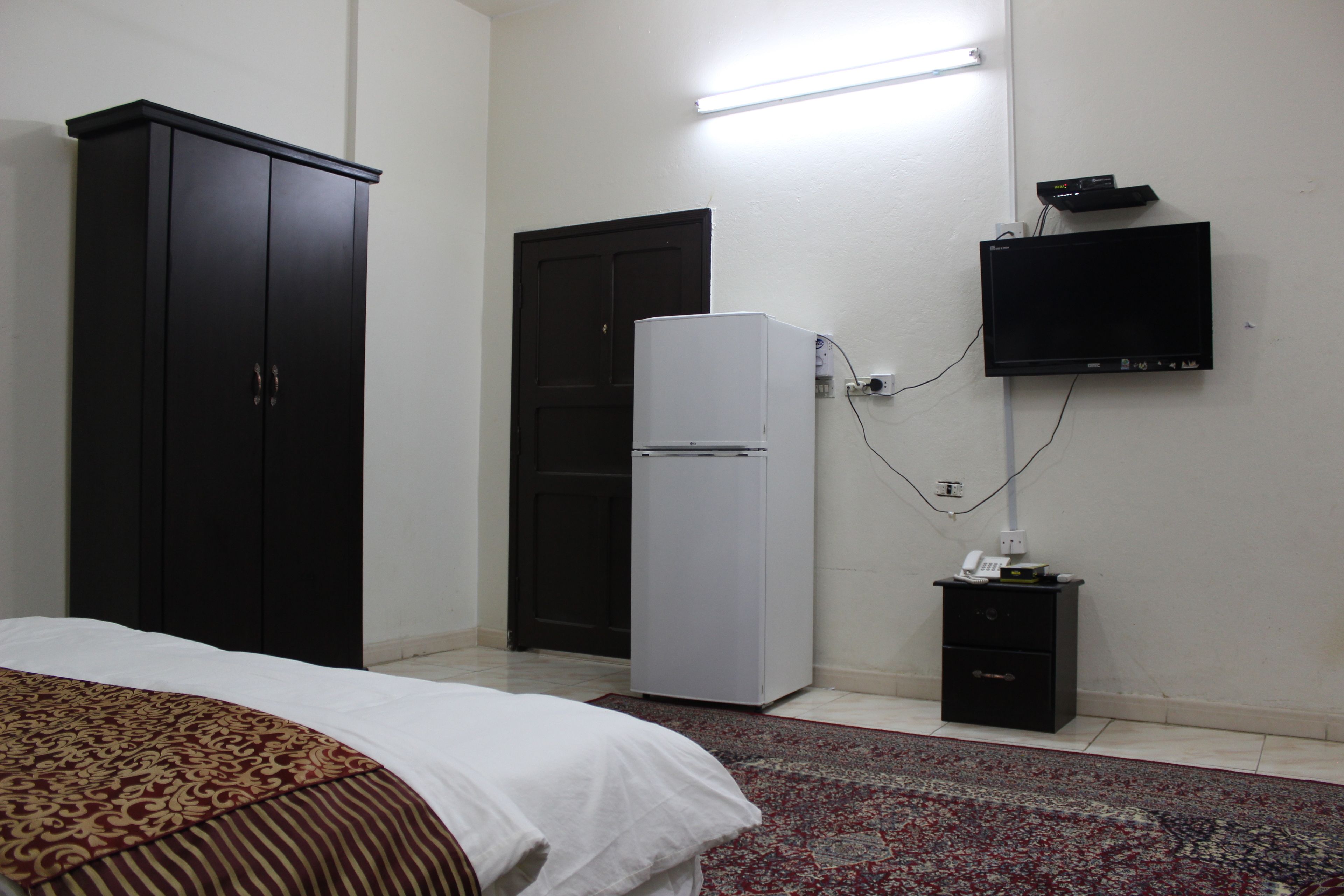 Quarto com cama, guarda-roupa, frigorífico, televisão e mesa de cabeceira.