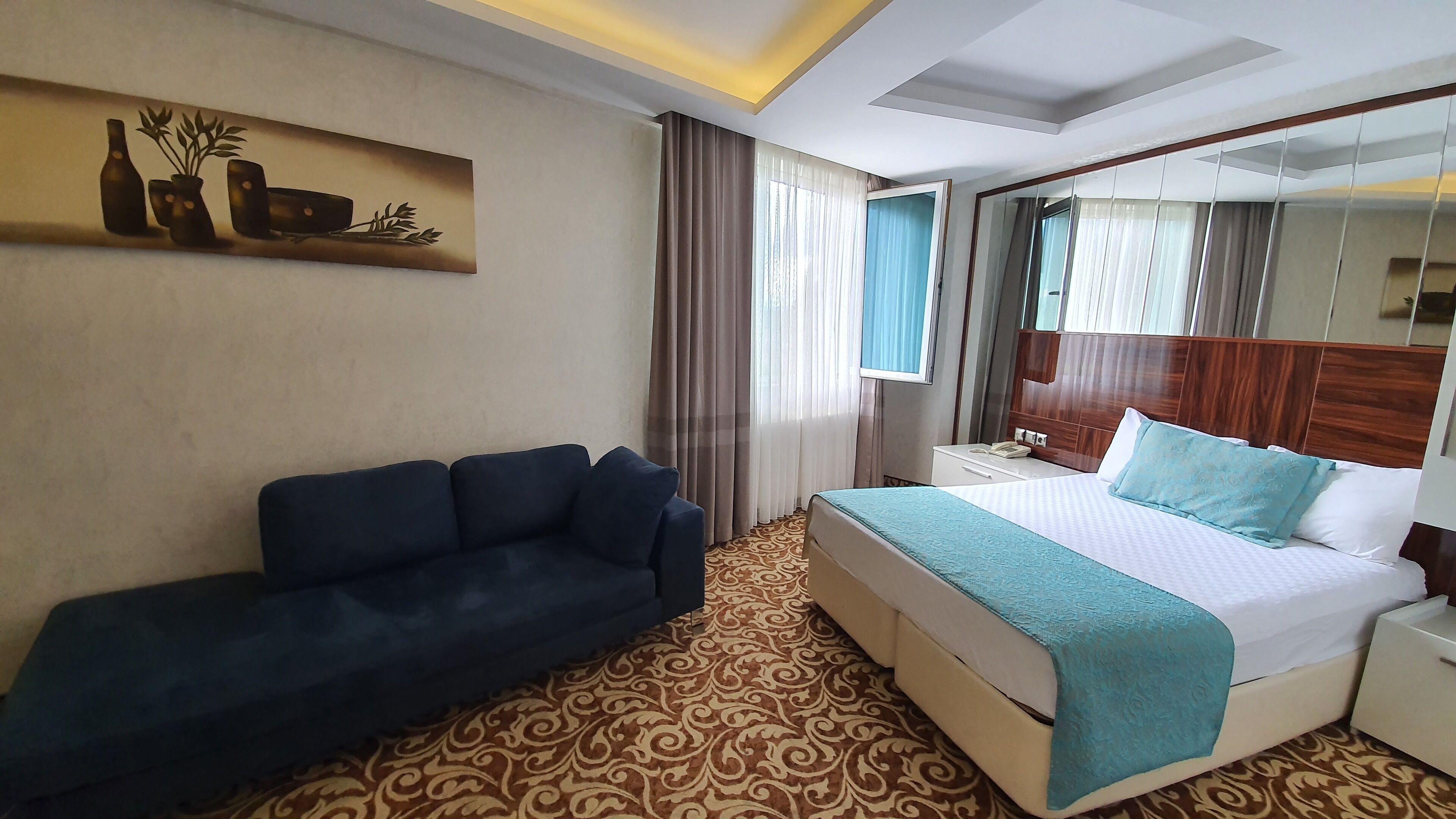 Quarto de hotel com cama, sofá, mesa de cabeceira, telefone e espelho.