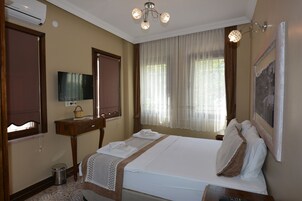 Quarto de hotel com cama, televisão, uma mesinha com cesta, janela com cortinas e ar condicionado.