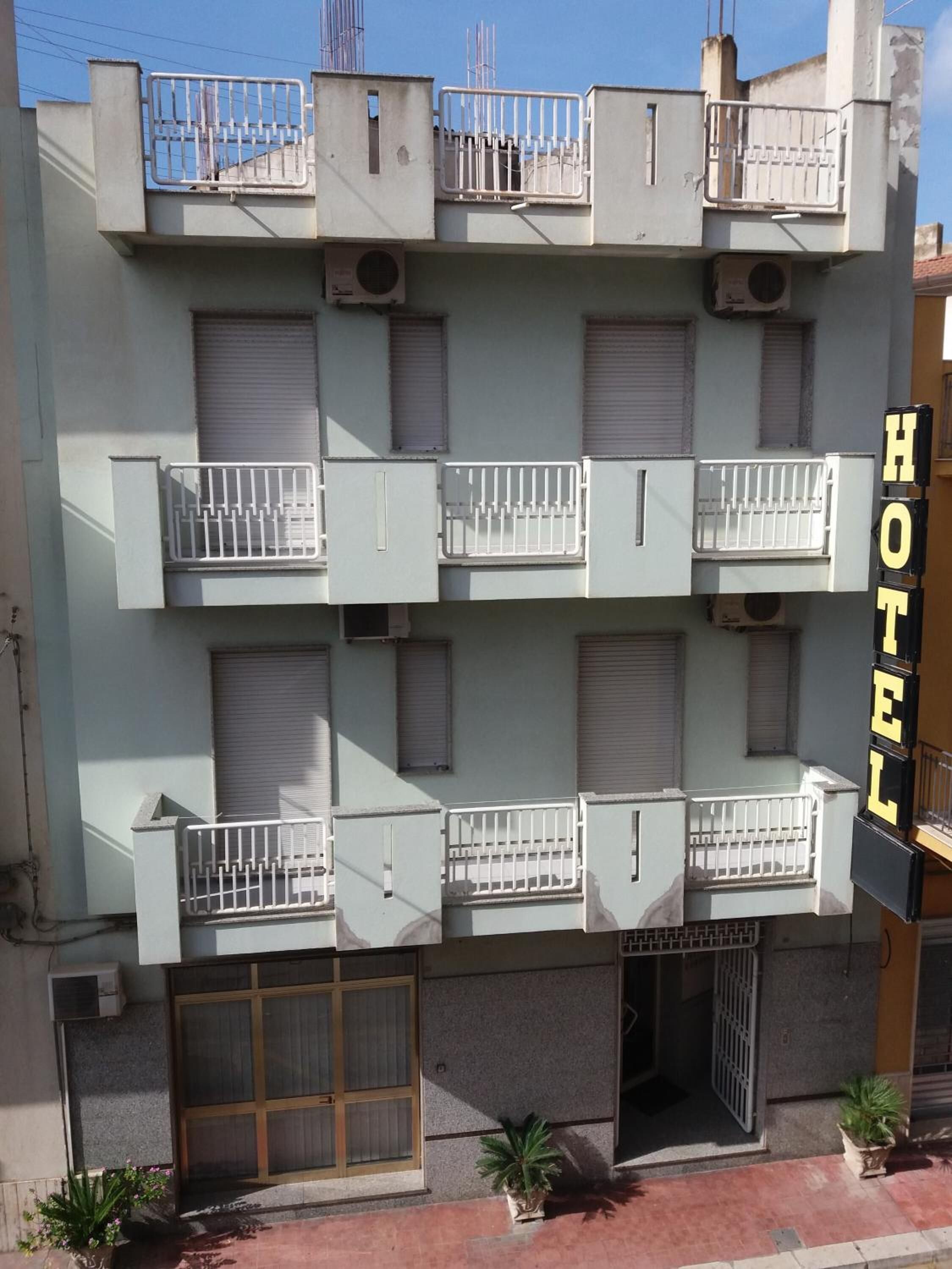 Um hotel de vários andares com varandas, aparelhos de ar condicionado e uma placa indicando ser um hotel.