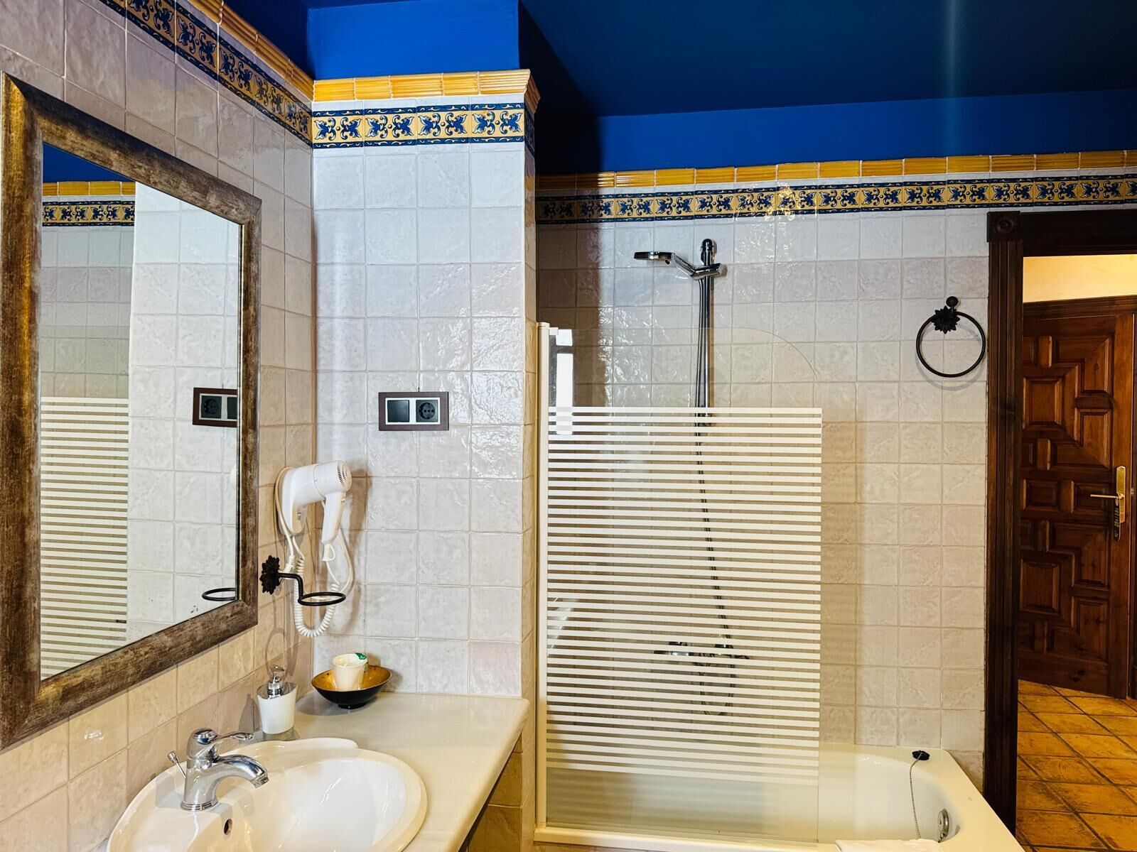 Casa de banho com lavatório, espelho, secador de cabelo e chuveiro com porta-toalhas.