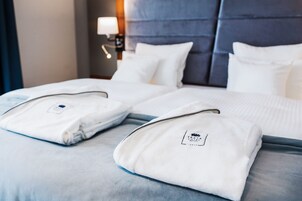 Quarto de hotel com duas camas, cada uma com toalhas brancas dobradas e o logotipo visível.