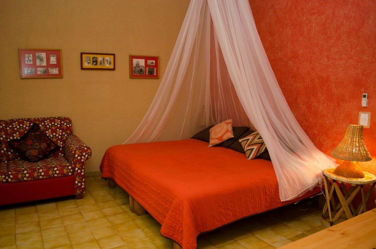 Quarto com cama sob dossel, sofá com almofadas estampadas e uma pequena mesa com luminária.