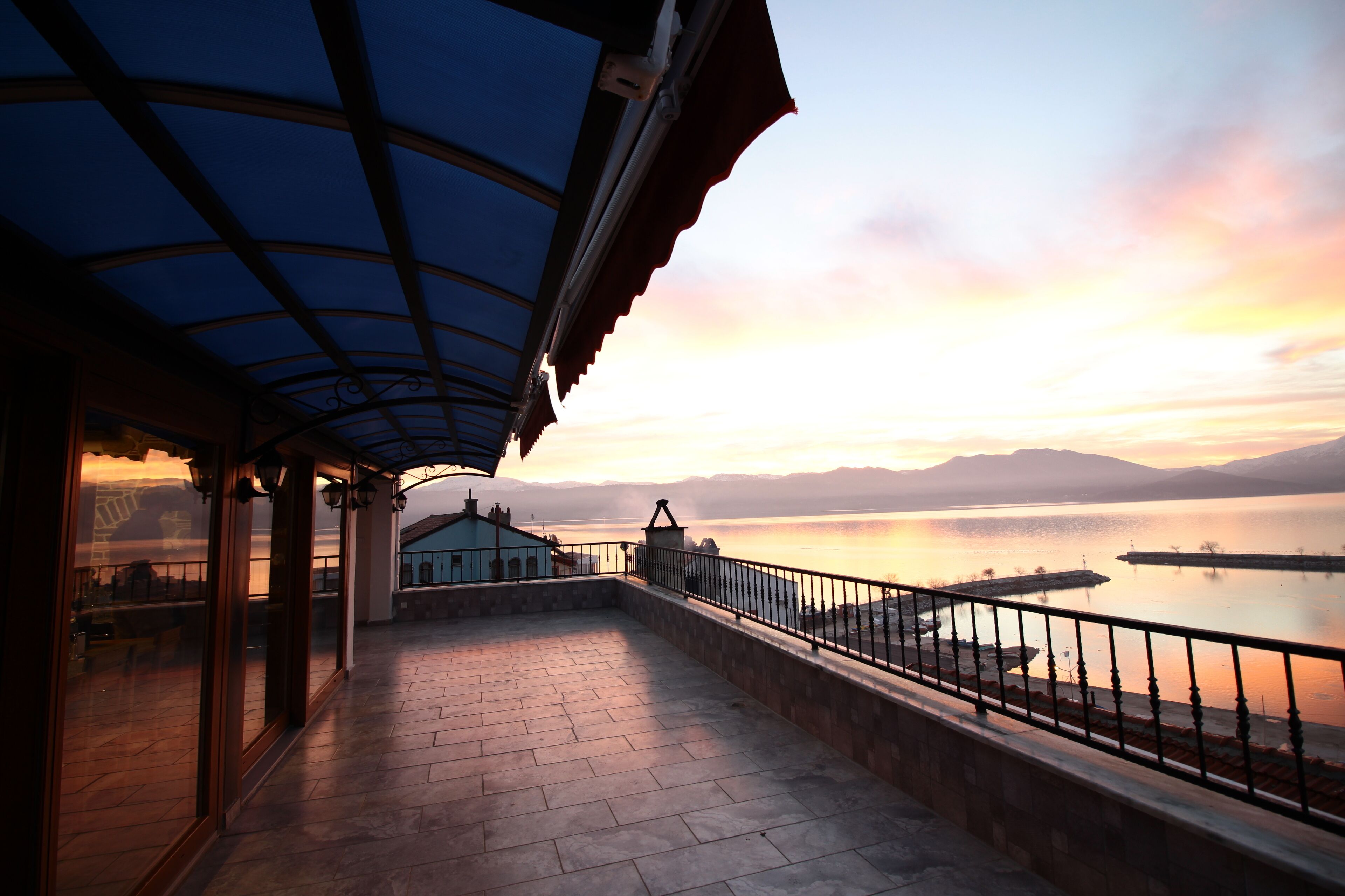 Terraço com vista para um lago tranquilo e montanhas ao pôr do sol.