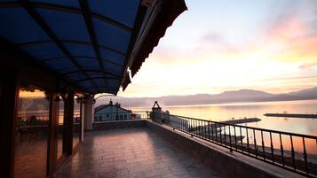 Terraço com vista para um lago tranquilo e montanhas ao pôr do sol.