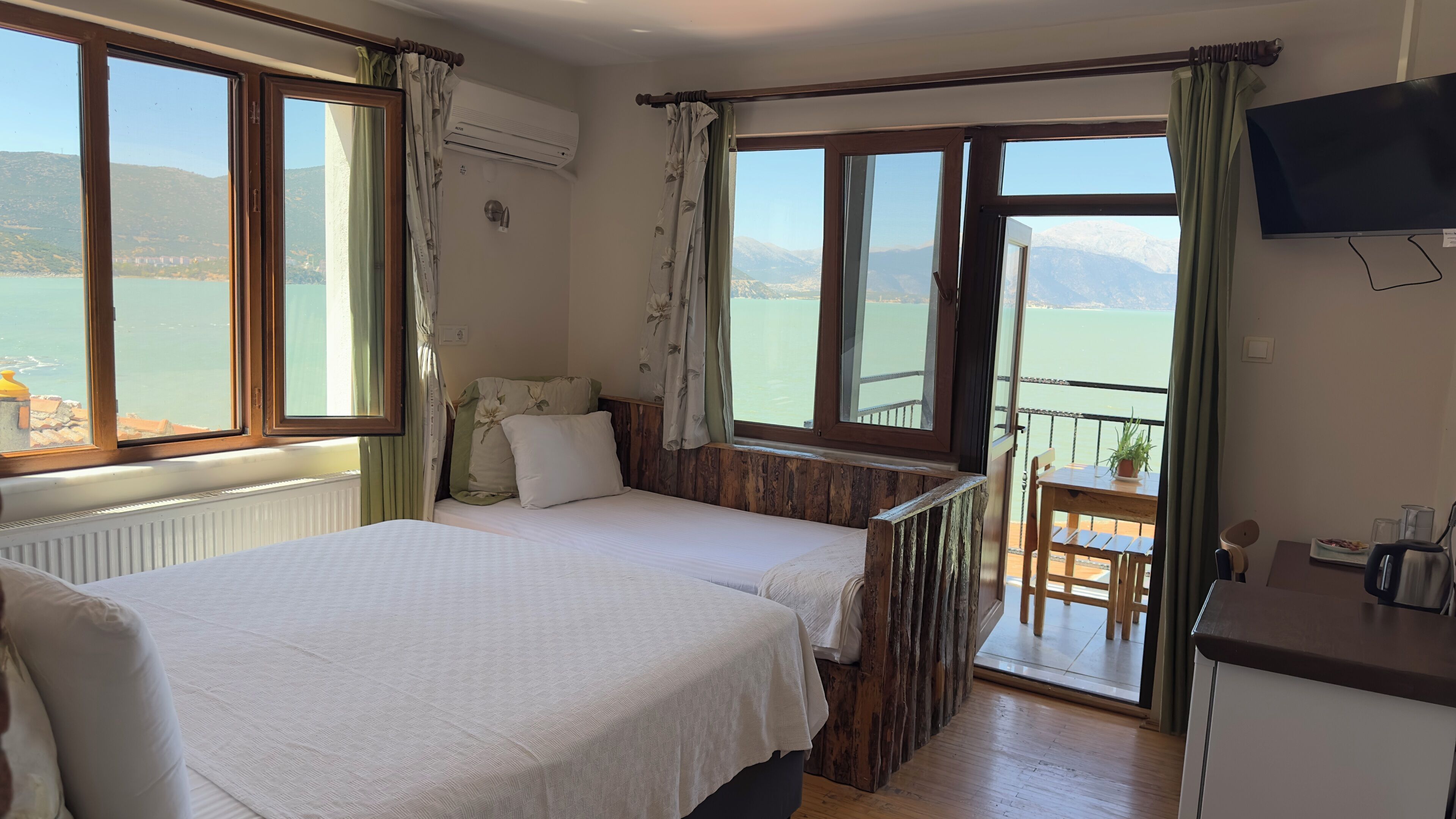 Quarto com cama, mesa pequena, televisão e varanda com vista para o mar.