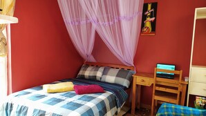 Quarto com uma cama, mesa de cabeceira, um laptop e uma pequena escrivaninha.