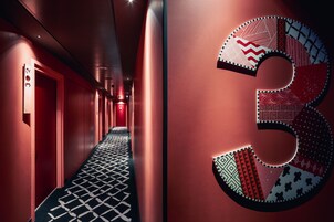 Um corredor com piso estampado, paredes vermelhas e um número '3' grande e iluminado.