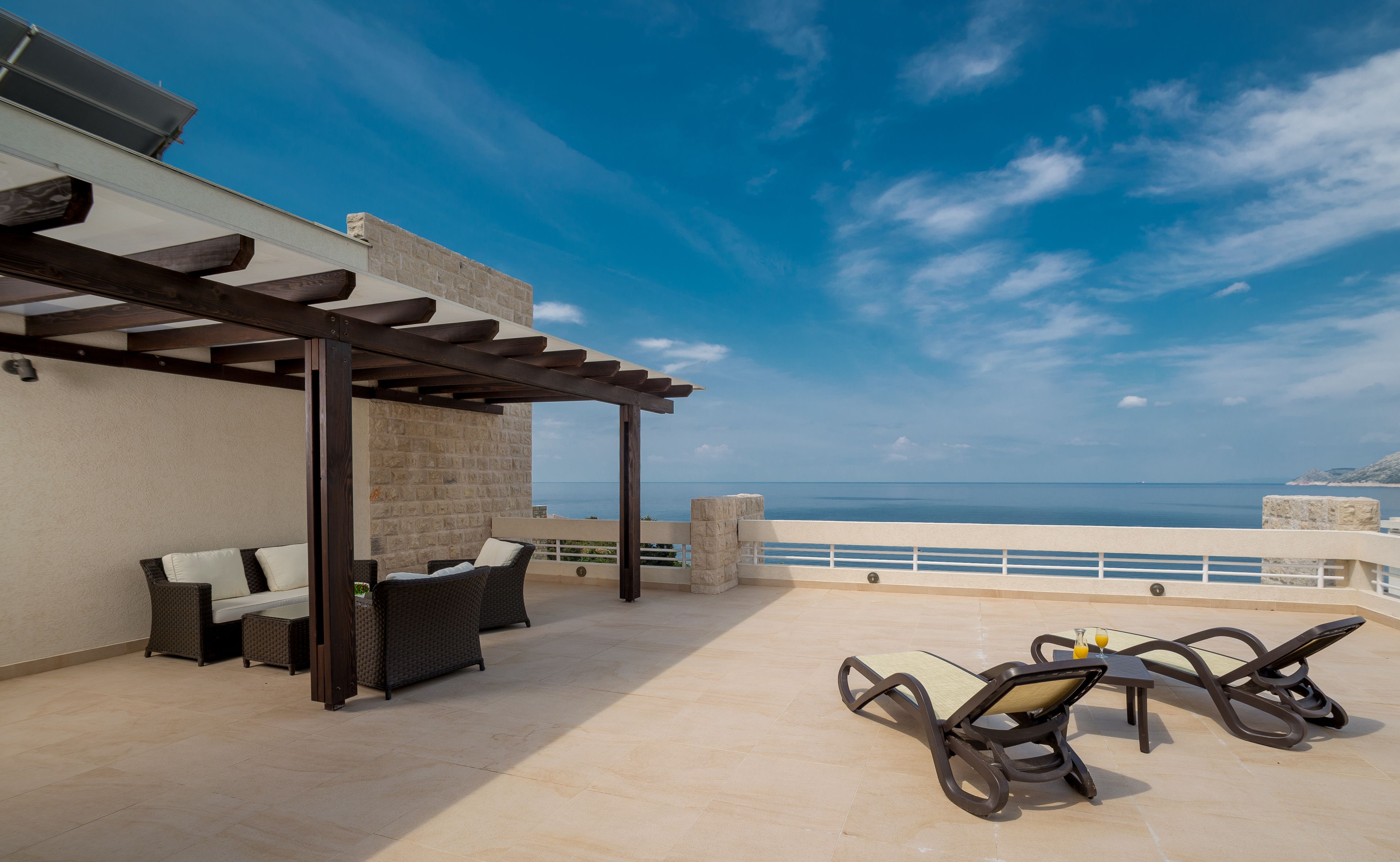 Um terraço com mobiliário de exterior, pérgula e vista para o mar.