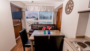 Espaço compacto com mesa de jantar, cadeiras, sofá, TV, cozinha e uma grande janela com vista para a cidade.