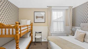 Quarto com cama beliche, cama de solteiro, cadeira, janela com cortinas e um quadro na parede.