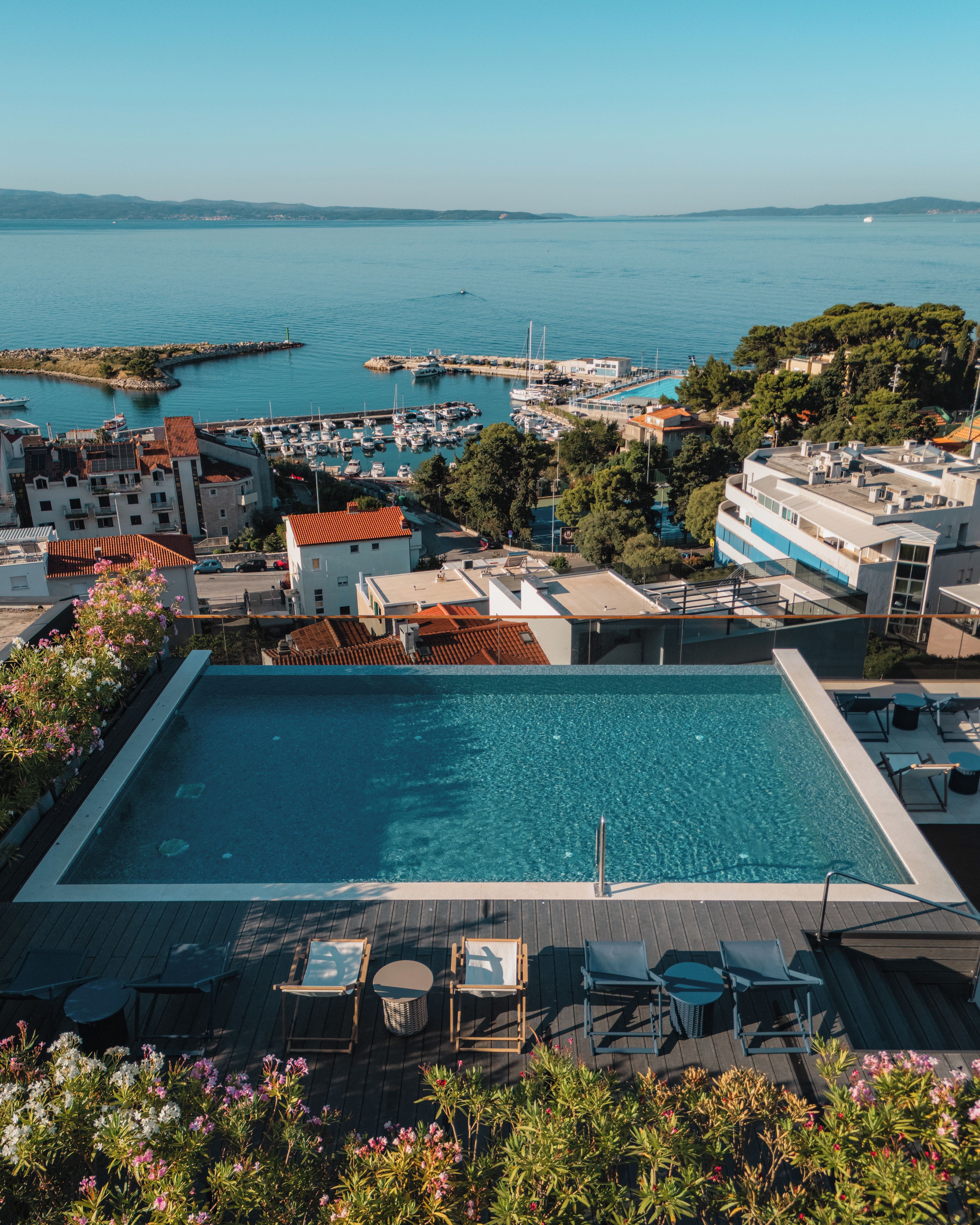 Piscina no terraço com água azul cristalina, rodeada por espreguiçadeiras e vista para o mar e a marina.