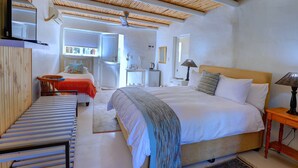 Quarto com cama, um banquinho, escrivaninha e espelho.