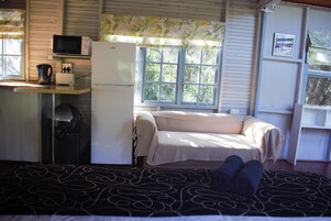 Quarto compacto com cama, pequeno espaço de cozinha e janela com cortinas.