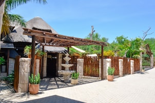 Entrada de um resort tropical com um edifício de telhado de palha, pérgola de madeira e cactos em vasos.
