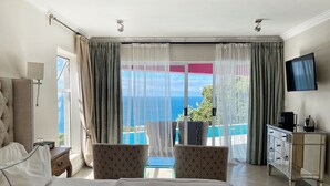 Quarto de hotel com cama, televisão, secretária com cafeteira e vista para o oceano.