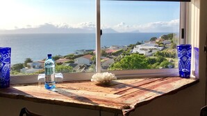 Quarto com vista para o mar, uma mesa com uma garrafa de água, duas cadeiras e uma tigela decorativa.
