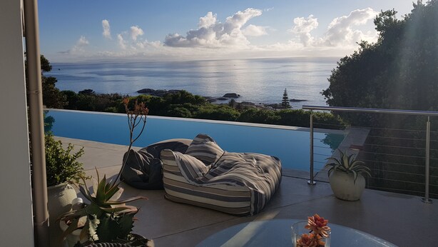 Uma varanda com vista para o mar, uma piscina e uma área de estar com almofadas listradas.