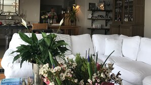 Uma sala de estar com um sofá branco, uma mesa de centro de madeira e um arranjo floral.