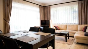 Uma sala de estar moderna com sofá, mesa de centro, televisão e área de refeições com cadeiras e mesa.