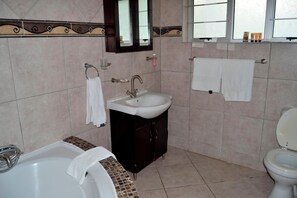 Casa de banho com banheira, lavatório e sanita. Toalhas penduradas na parede e uma janela acima do lavatório.