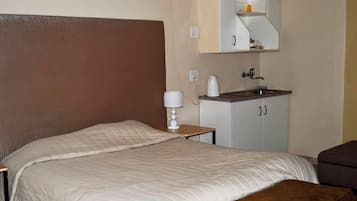 Quarto de hotel com cama, mesa de cabeceira, luminária, móvel pequeno com pia e uma cadeira.