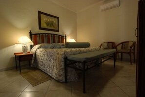Um quarto com uma cama, duas mesas de cabeceira com abajures, uma cadeira e um quadro na parede.