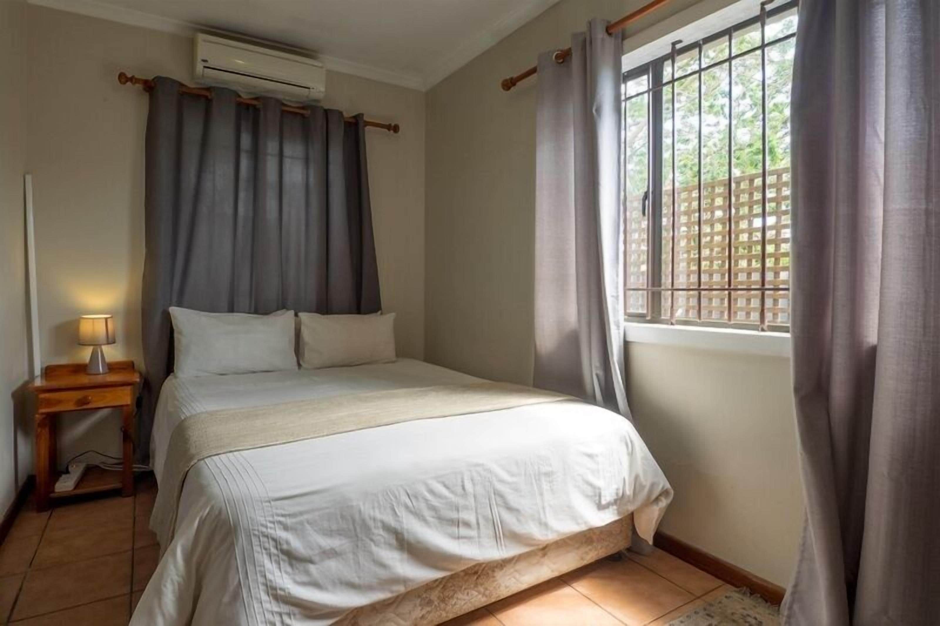 Quarto com cama, mesa de cabeceira, ar condicionado e janela com cortinas.