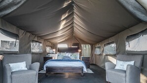 Um quarto com tenda, uma cama, duas poltronas, uma mesinha de cabeceira e uma janela.