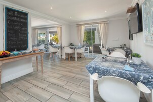 Uma área de refeições com um cardápio em lousa, uma mesa com toalha estampada e vista para o exterior.