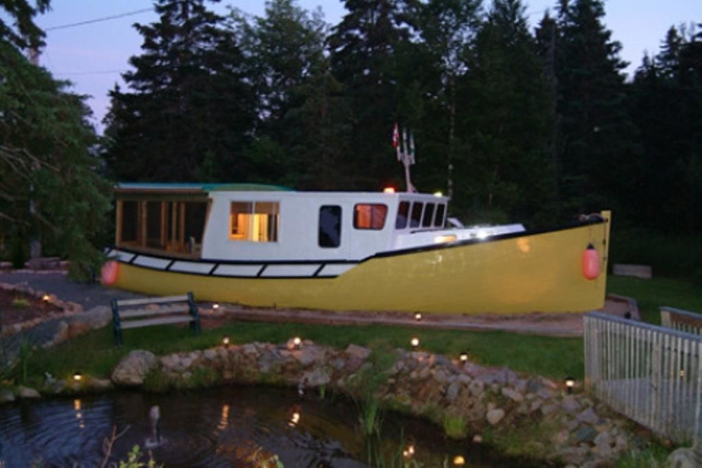 Um barco amarelo com cabine, atracado perto de um pequeno lago com uma ponte.
