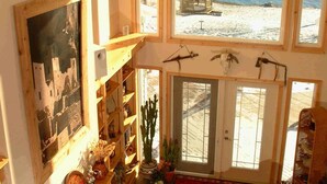 Uma sala de estar ampla com teto alto, grandes janelas com vista para a praia, lareira e diversos objetos decorativos.