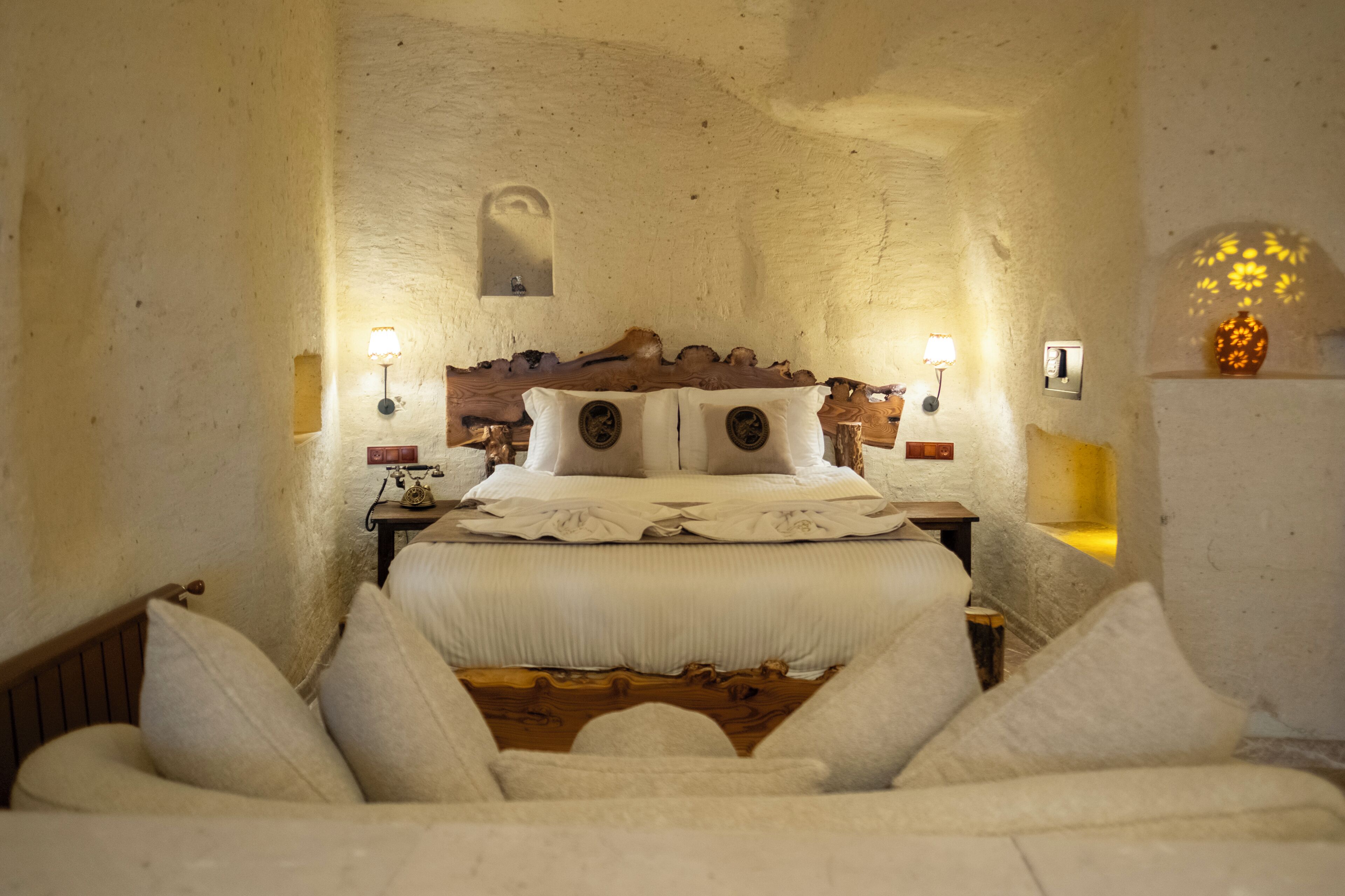 Um quarto aconchegante com cabeceira de madeira, uma cama grande com roupa de cama branca e duas luminárias fixadas na parede.