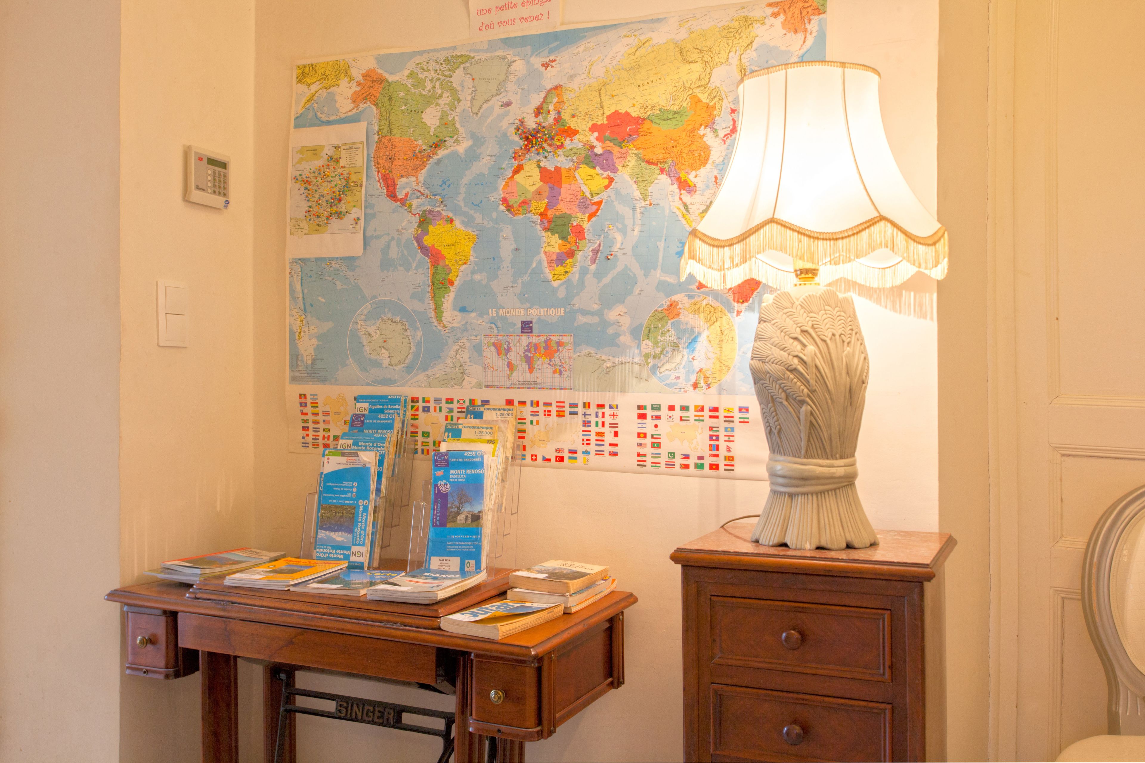 Uma mesa com um mapa-múndi, uma luminária e diversos livros.