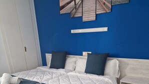 Cama bem arrumada com roupa de cama branca e azul, cabeceira de madeira e uma pequena mesa de cabeceira.