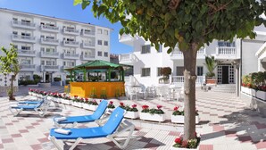 Um pátio de hotel com espreguiçadeiras, um pequeno quiosque e um edifício com varandas.