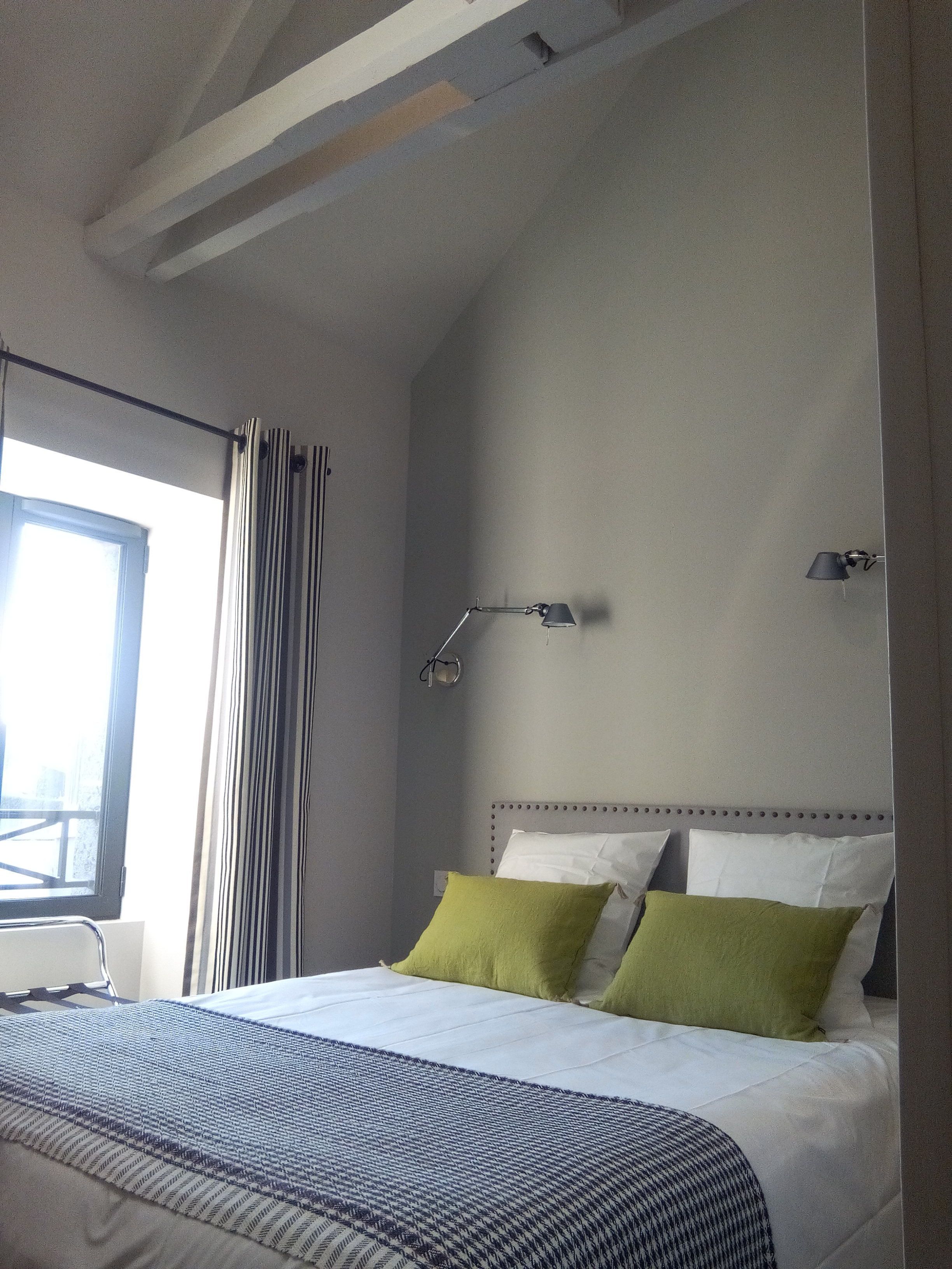 Quarto de hotel com cama, duas luminárias de cabeceira, janela com cortinas e vista para o exterior.