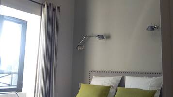 Quarto de hotel com cama, duas luminárias de cabeceira, janela com cortinas e vista para o exterior.