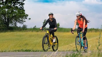 Dois ciclistas em um caminho pavimentado em um campo gramado, com árvores ao fundo.