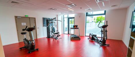 Academia com máquinas de cardio, equipamentos de peso e piso de madeira vermelha.